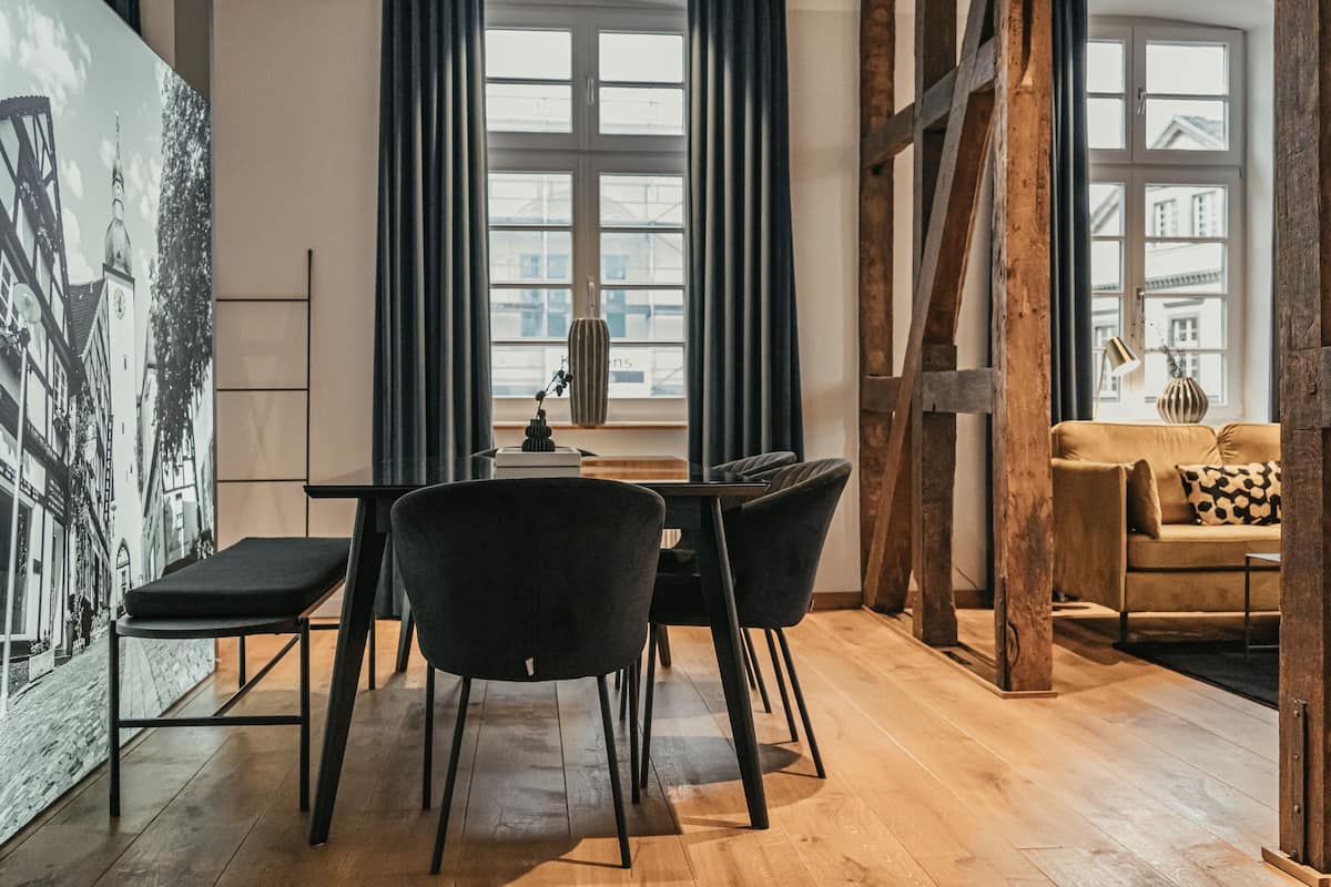 Uma sala de estar moderna com piso de madeira, uma área de jantar com mesa e cadeiras, e uma janela grande com cortinas.