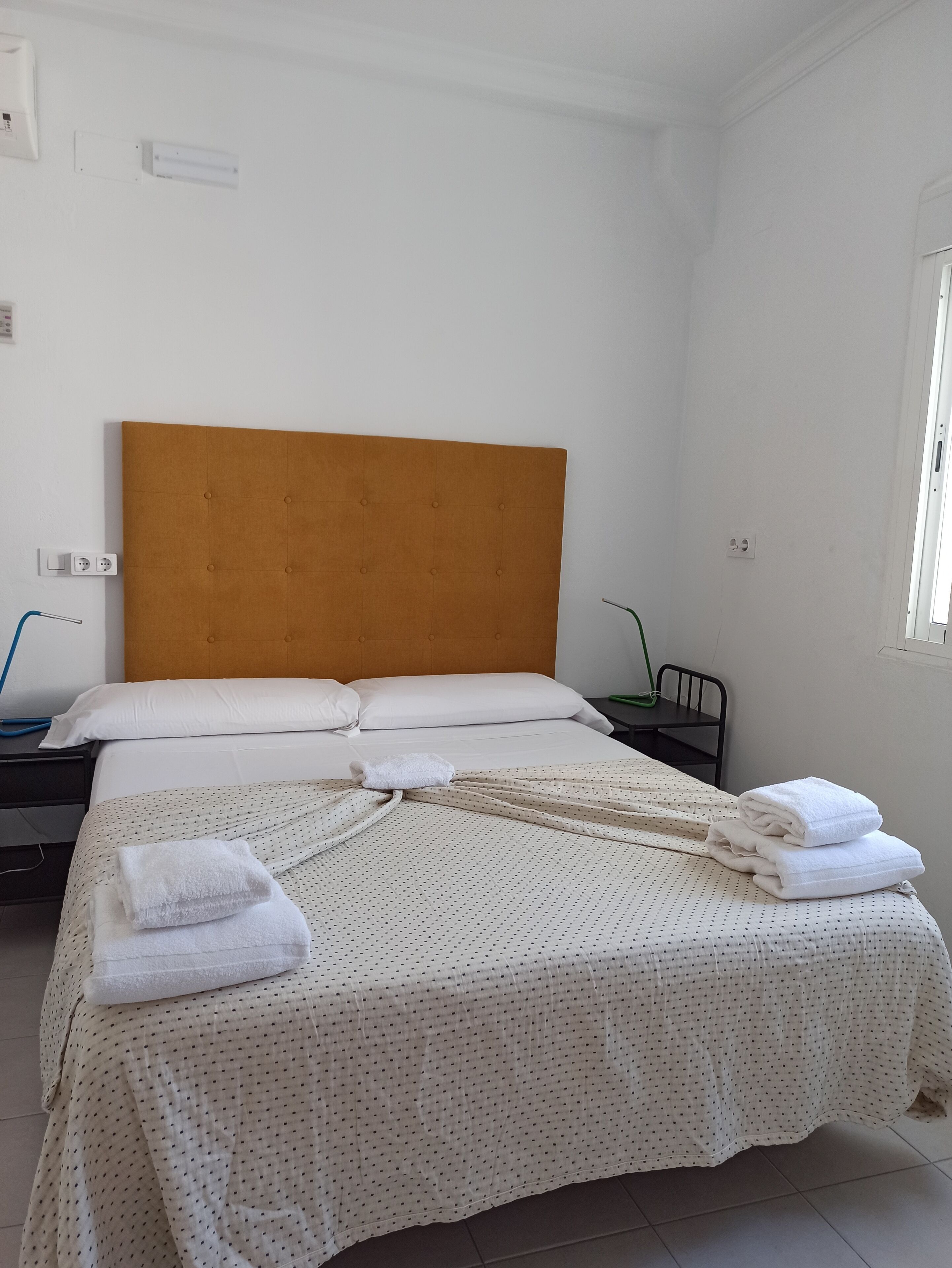 Uma cama bem arrumada com colcha de bolinhas, travesseiros brancos e uma toalha branca dobrada ao lado.