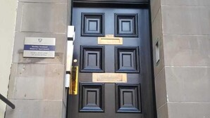 Uma porta preta com puxador dourado e uma placa acima que diz '18 Hanover Street'.