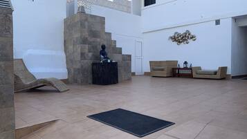 Uma área externa ampla com uma estátua de pedra, uma poltrona de vime, um sofá acolchoado e um objeto decorativo na parede.