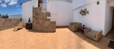 Um pátio espaçoso com escadaria de pedra, móveis de vime e um muro decorativo.