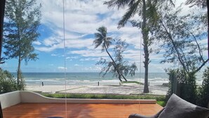 Uma varanda com vista para a praia, uma cadeira de lounge e uma pequena mesa.