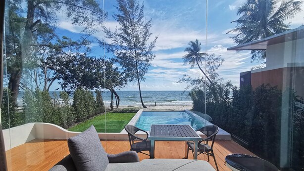 Uma área de estar moderna ao ar livre, com piscina, vista para o oceano e palmeiras.