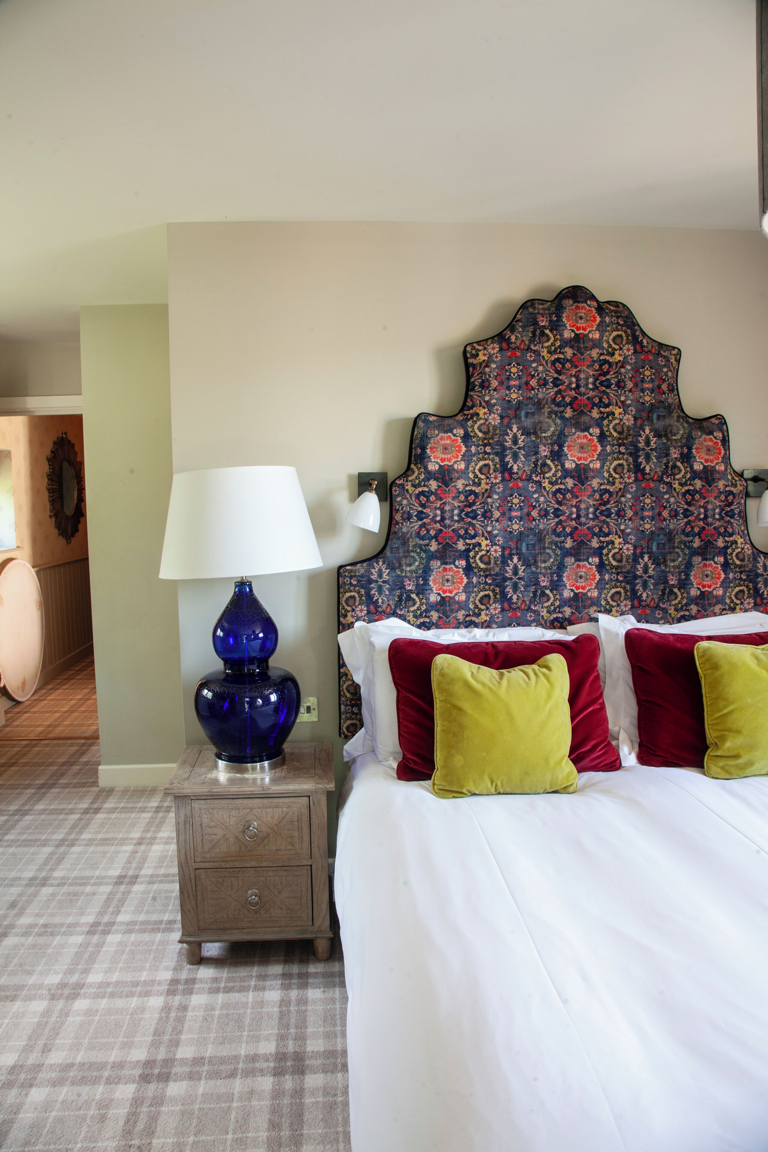 Quarto com cama, mesa de cabeceira, abajur e cabeceira estampada.