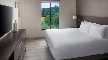 Quarto de hotel moderno com uma cama grande, televisão de tela plana, cômoda e janela com vista para uma floresta.
