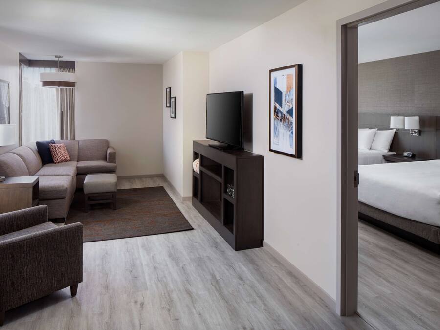 Quarto de hotel com sofá, televisão, cama e pequena escrivaninha.