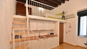 Uma cozinha compacta com escada de madeira, armários brancos, micro-ondas e uma pia pequena.
