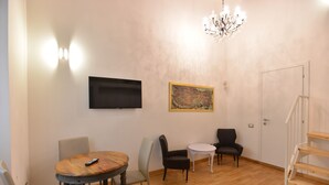 Uma sala de estar com televisão, um quadro, um candelabro e uma escada.