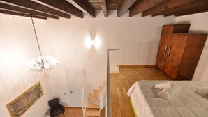 Um quarto com cama, escada de madeira, lustre, guarda-roupa e um quadro na parede.