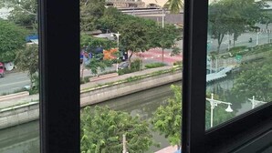 Vista de uma paisagem urbana através de uma janela, incluindo um edifício com telhado curvo, um rio e uma ponte.