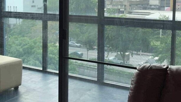 Quarto moderno com amplas janelas do chão ao teto, um sofá de couro e vista para o horizonte urbano.
