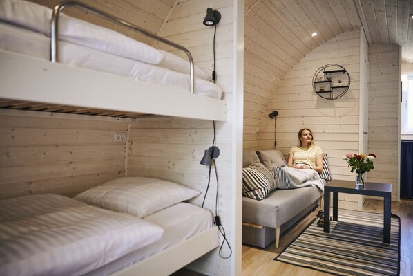 Uma cama beliche com escrivaninha e sofá em quarto estilo cabana, com paredes de madeira e teto curvo.