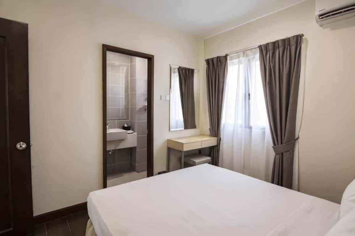 Quarto de hotel com cama, mesinha de cabeceira, espelho, janela com cortinas e ar condicionado.