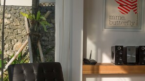 Uma sala de estar moderna com uma poltrona de couro preto, uma pequena mesa de madeira, um abajur e uma obra de arte emoldurada na parede.