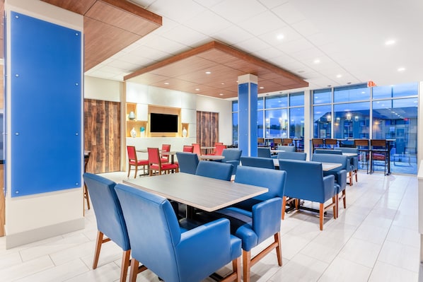 Uma sala de jantar moderna com cadeiras estofadas em azul, mesas de madeira e uma grande janela com vista para o exterior.