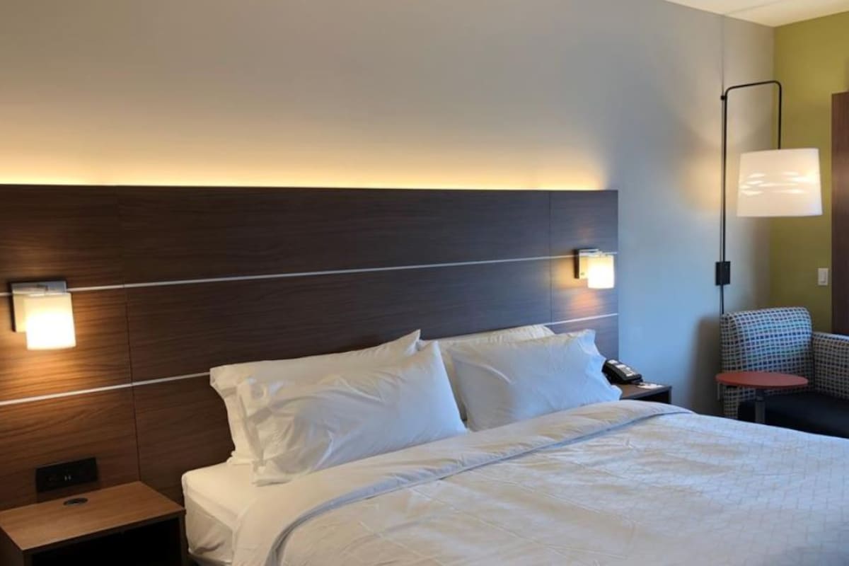 Quarto de hotel com uma cama grande, mesas de cabeceira, uma luminária na parede e uma janela com vista.