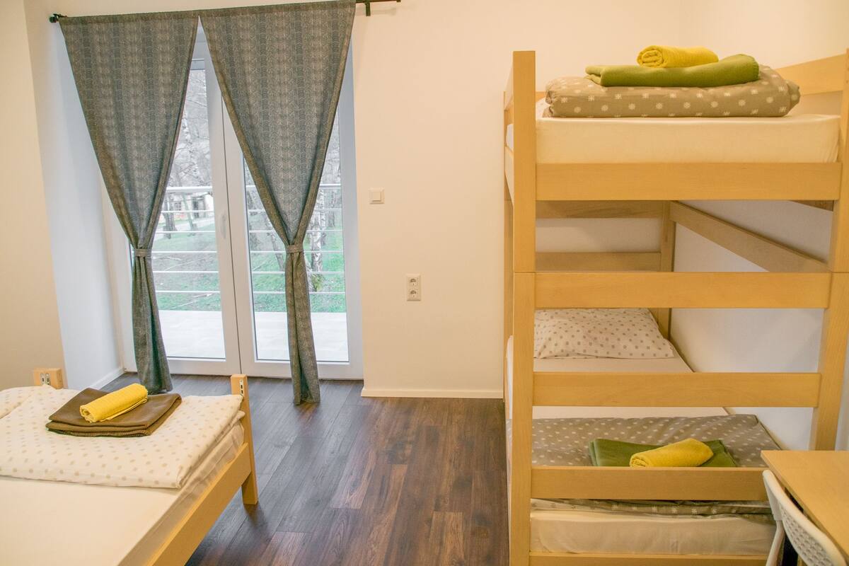 Quarto com uma cama, uma beliche e uma janela com cortinas.