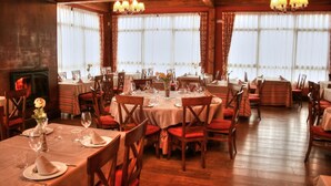 Restaurante com várias mesas redondas, cada uma com toalhas brancas, cadeiras estofadas vermelhas e copos de vinho.