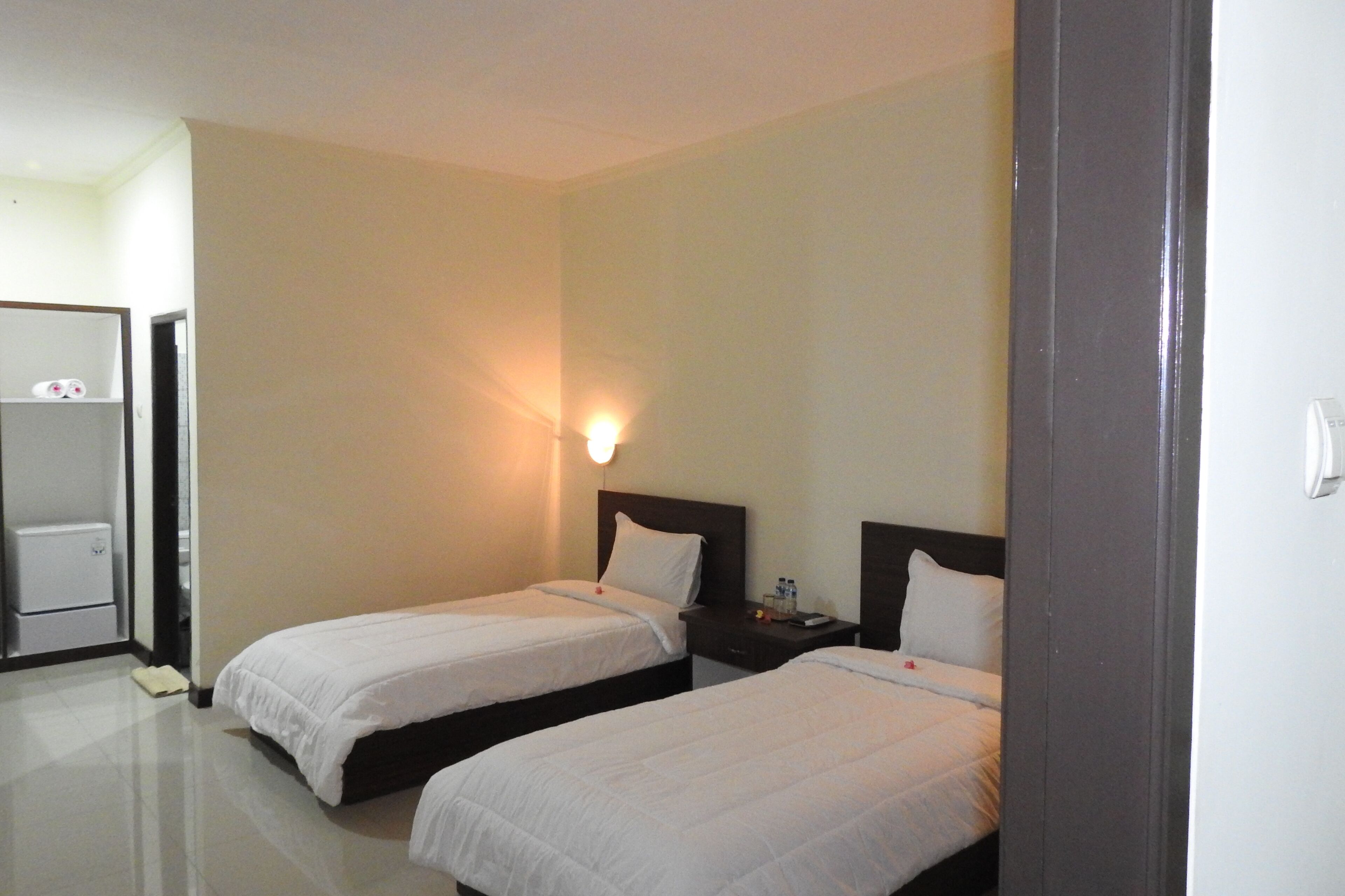 Quarto de hotel com duas camas de solteiro, mesa de cabeceira e luminária fixada na parede.