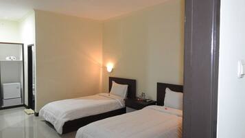 Quarto de hotel com duas camas de solteiro, mesa de cabeceira e luminária fixada na parede.