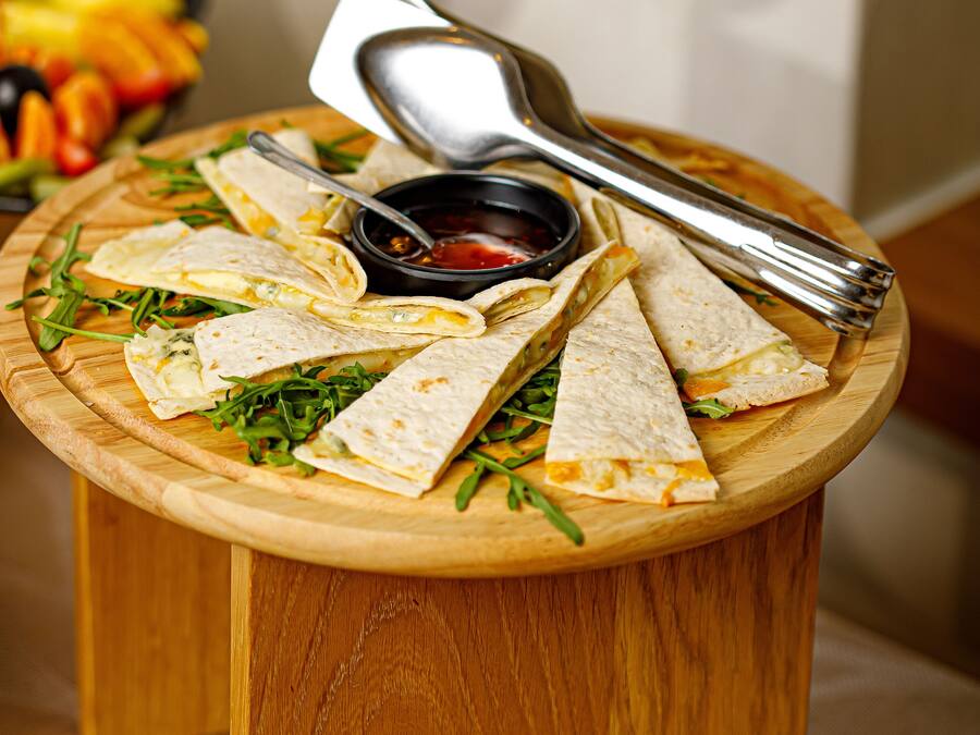 Uma mesa de madeira com um prato de quesadillas e uma tigela de molho.