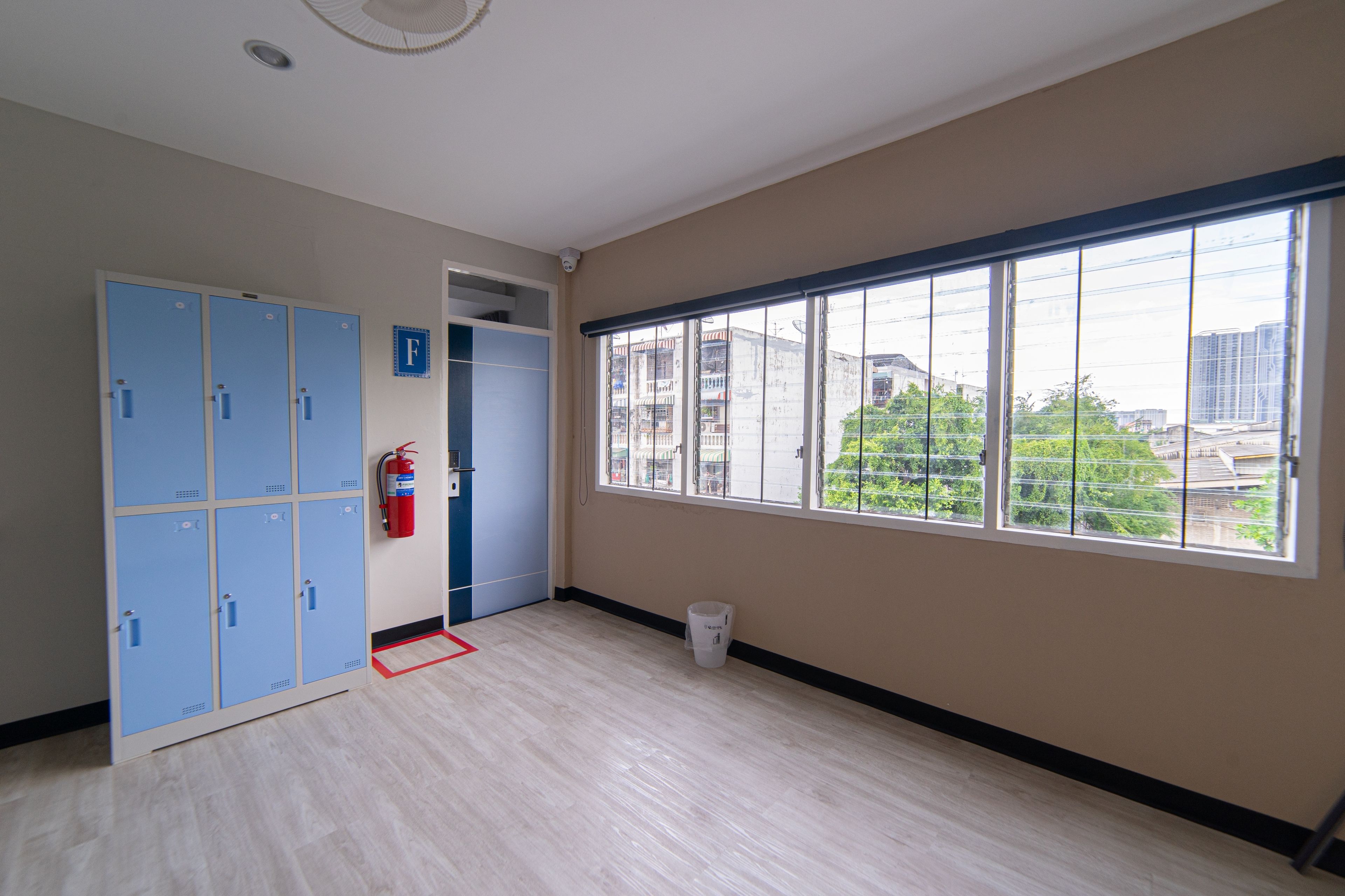 Quarto com uma janela grande, área com armários azuis e um extintor de incêndio.