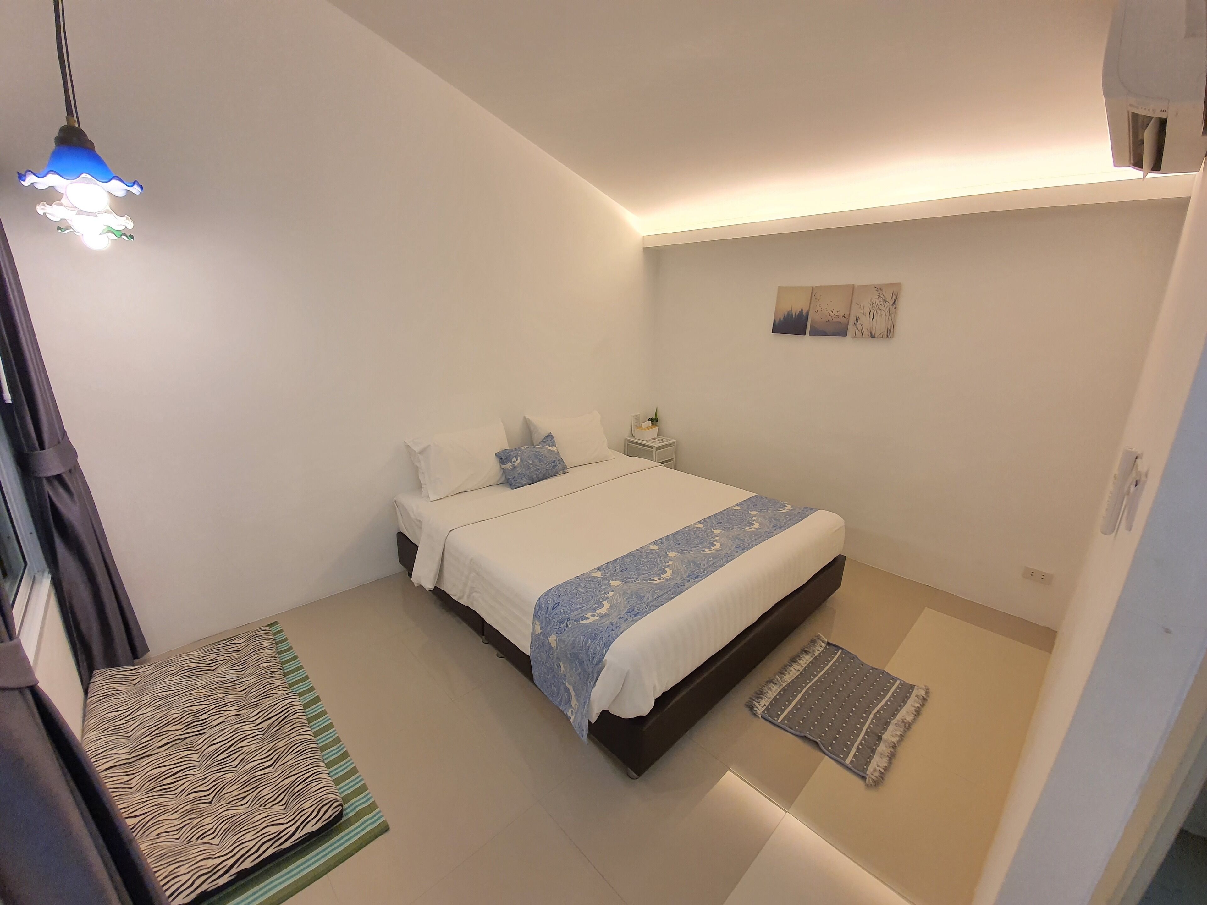 Quarto com cama, mesa de cabeceira, abajur e tapete.
