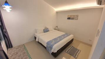 Quarto com cama, mesa de cabeceira, abajur e tapete.