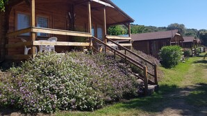 Uma cabana de madeira com varanda, rodeada por um jardim com flores roxas e brancas.