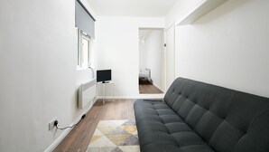 Uma sala de estar moderna com um sofá cinzento, uma mesinha com uma TV e um tapete estampado.
