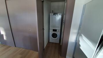 Uma lavanderia compacta com máquina de lavar e secadora, piso de madeira e uma porta que dá para outro cômodo.