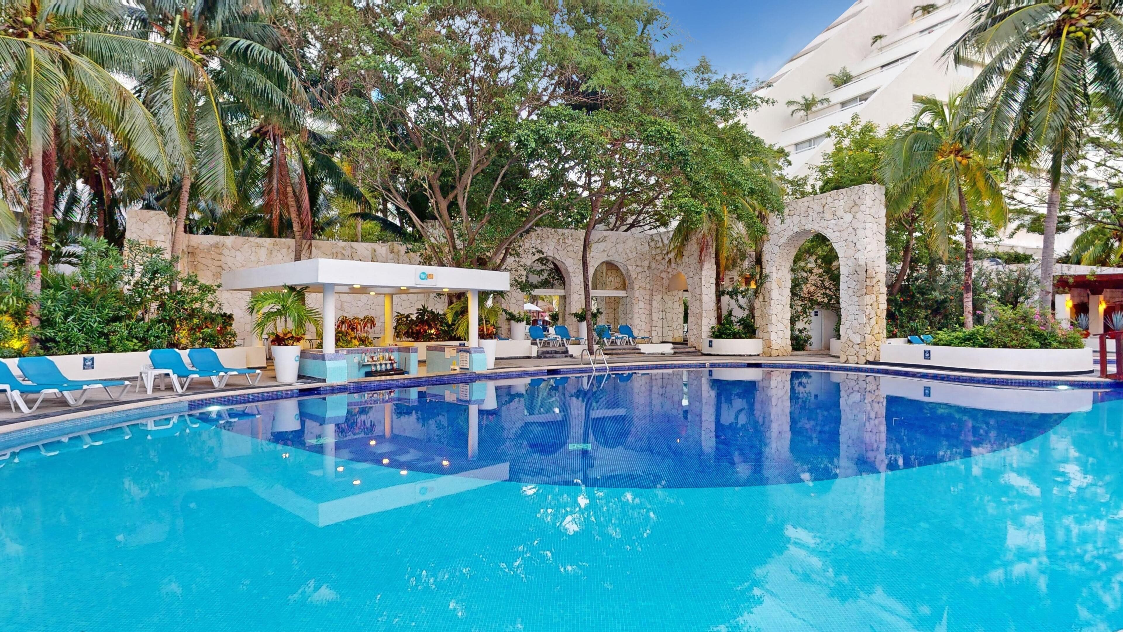 Piscina com cadeiras de praia e um arco de pedra.