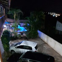 Vista noturna de um bairro residencial com piscina, carros estacionados e vegetação ao redor.