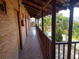 Um corredor coberto com parede de tijolos, um extintor de incêndio e vista para uma piscina e vegetação.