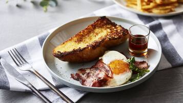 Um prato com torradas, bacon e ovo frito, acompanhado por uma pequena chávena de chá.