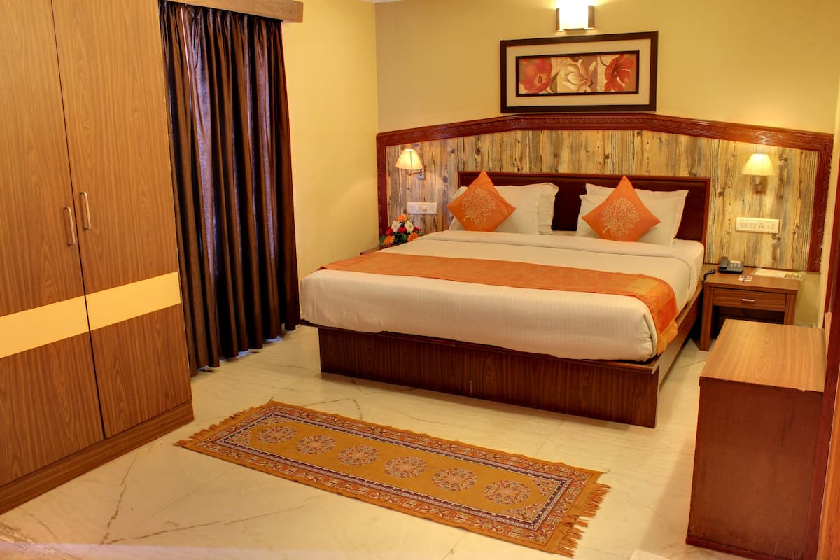 Quarto de hotel com uma cama grande, cabeceira de madeira, mesa de cabeceira com abajur, guarda-roupa de madeira e tapete estampado.
