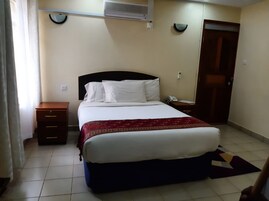 Quarto com cama, mesas de cabeceira, telefone e uma porta.