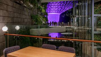 Um espaço interno moderno com guarda-corpo de vidro, mesa de madeira e cadeiras hexagonais roxas.