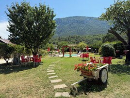 Um jardim com cadeiras e mesas vermelhas, uma piscina e uma montanha ao fundo.