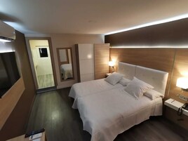 Quarto de hotel moderno com uma cama grande, mesas de cabeceira, uma TV e um espelho.