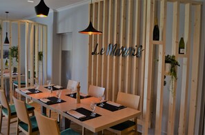 Uma área de refeições com uma mesa comprida posta para seis pessoas, paredes com ripas de madeira, luminárias pendentes e um display de garrafas de vinho fixado na parede.