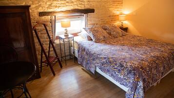 Quarto com cama de madeira, mesa de cabeceira com abajur, cadeira e escada de madeira encostada em uma parede de pedra.