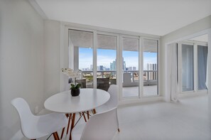 Quarto moderno com uma janela grande, uma mesa redonda e cadeiras brancas.