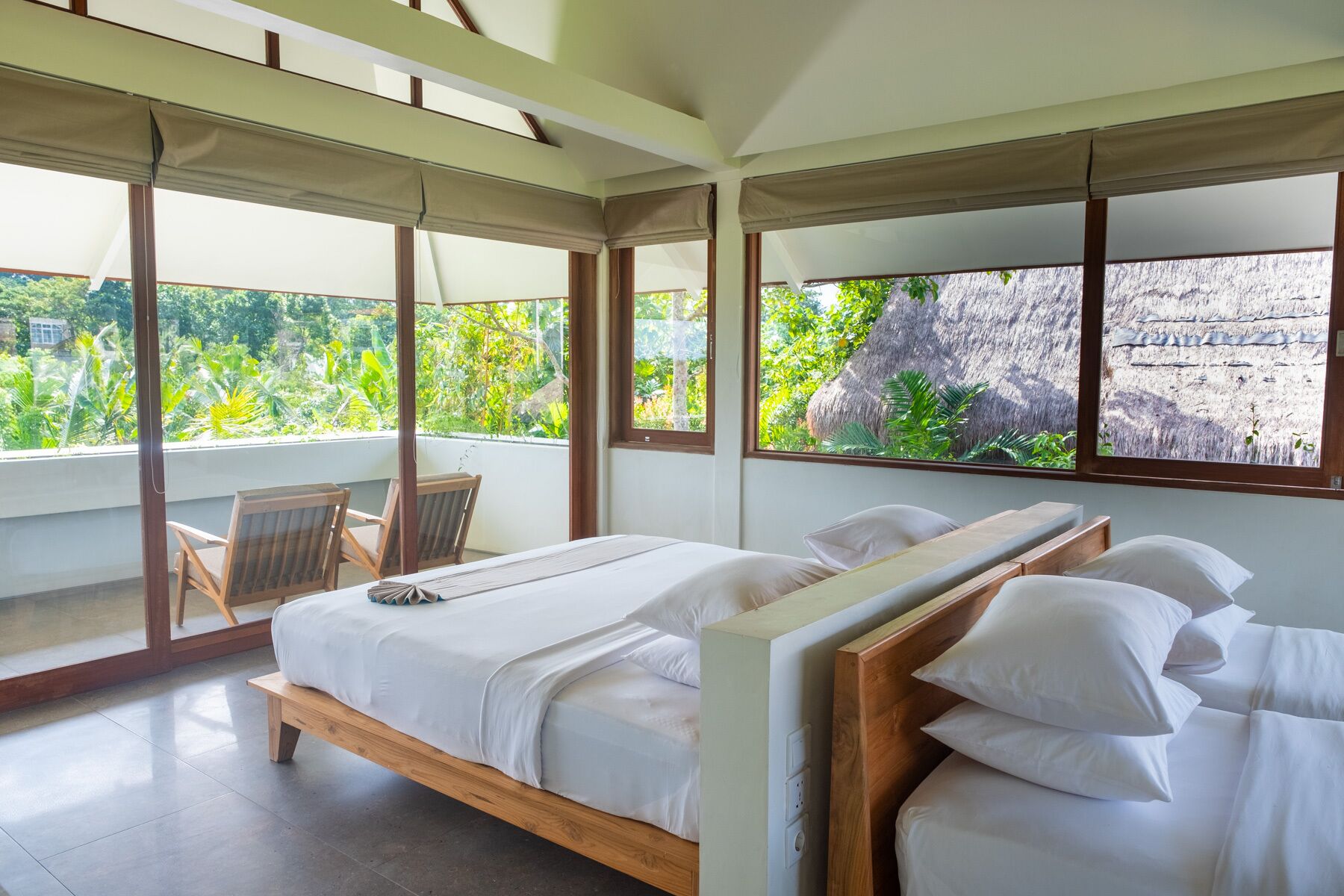 Quarto com cama, cadeira e vista para o verde lá fora.