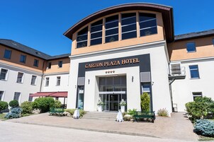 Um hotel com telhado curvo, uma placa com a inscrição 'GARZON PLAZA HOTEL' e entrada pavimentada com um banco e plantas em vasos.