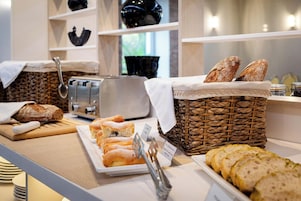 Buffet de café da manhã com diversos pães e doces, uma torradeira e uma cesta de vime.