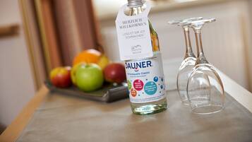Uma garrafa de água mineral DAUNER com etiqueta, um prato de frutas e dois copos de vinho vazios sobre uma mesa.