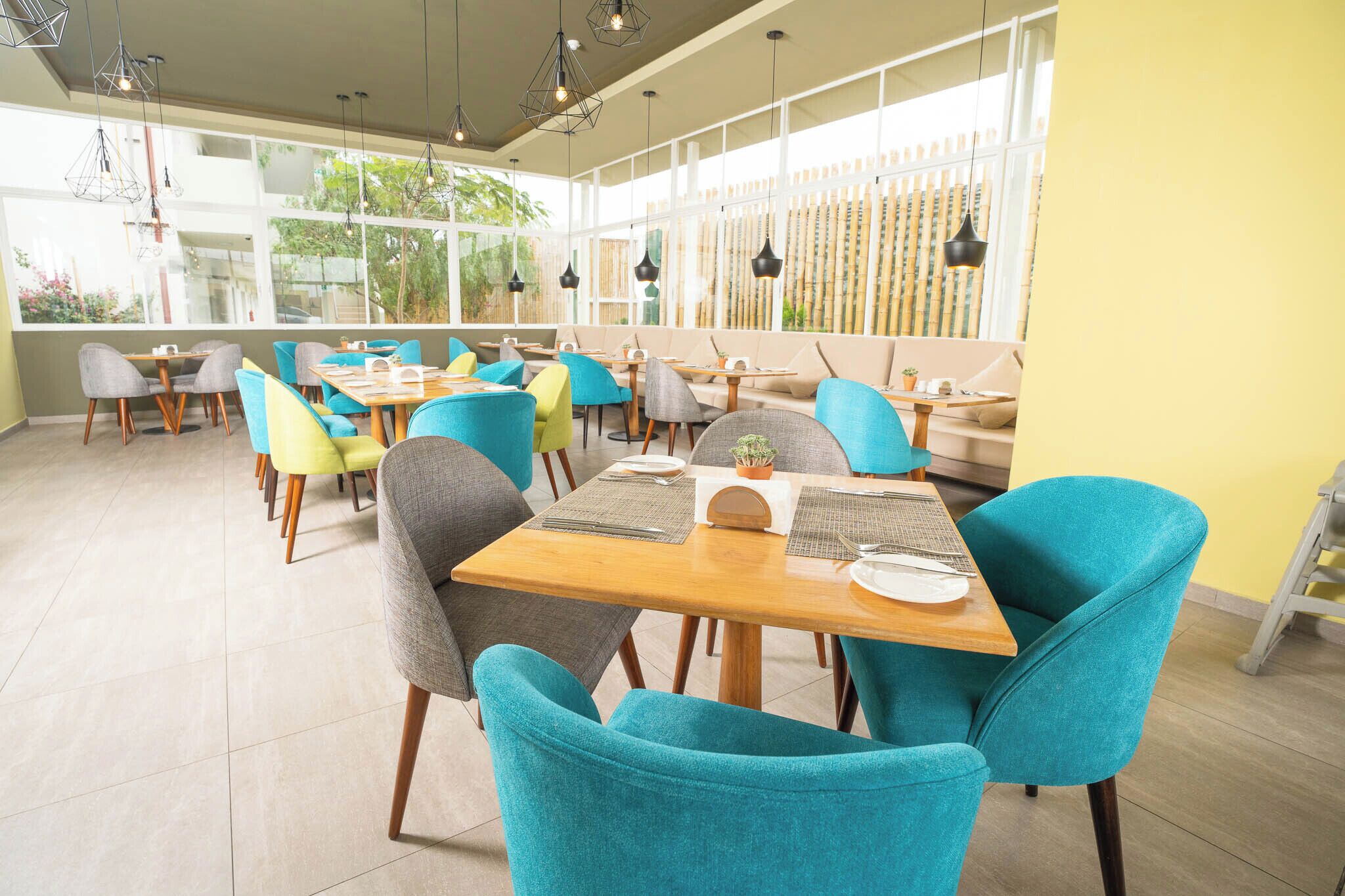 Um restaurante com cadeiras azul-turquesa e cinzentas, mesas de madeira e luminárias pendentes.