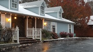 Uma casa de dois andares com varanda, luzes de festa e telhado coberto de neve.