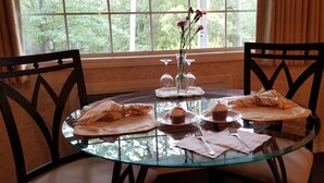 Uma mesa de vidro redonda com um vaso de flores, dois pratos com comida e duas cadeiras.